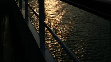 Um barco em um rio, com montanhas em ambas as margens e o sol se pondo ao fundo.