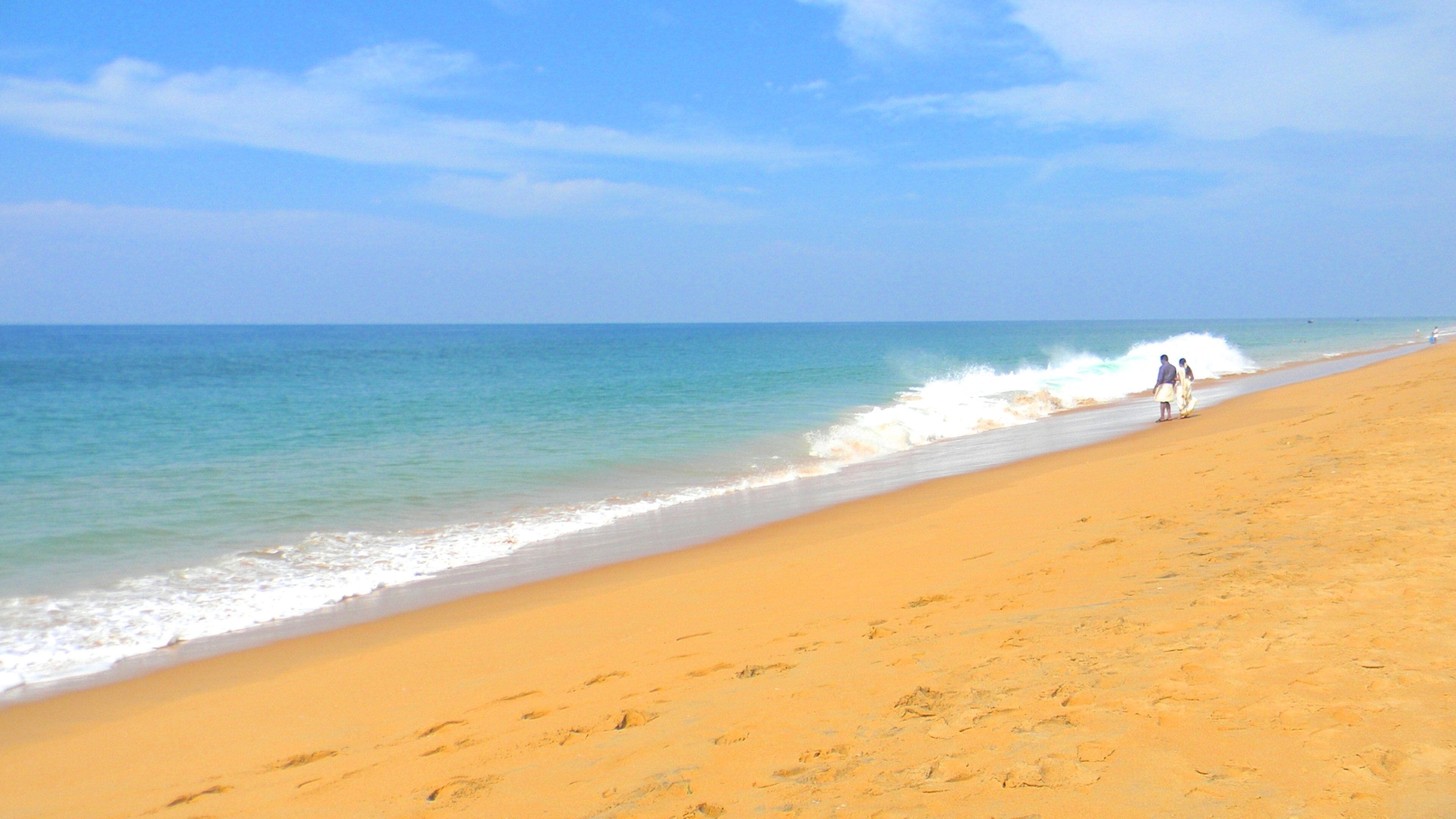 Uma praia arenosa com ondas suaves e céu claro.