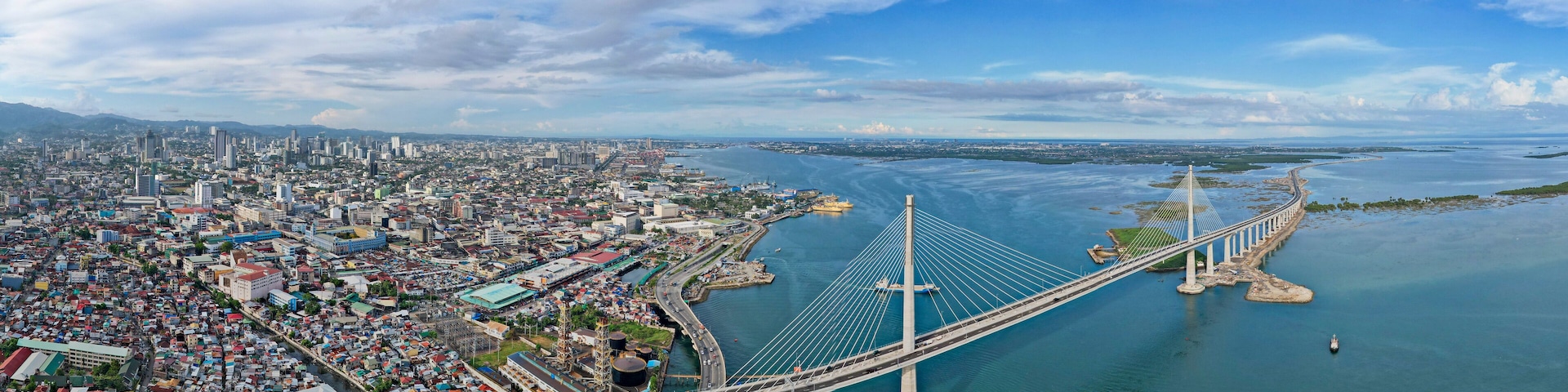 Uma extensa ponte suspensa atravessa um rio largo, com uma cidade densamente povoada de um lado e água aberta do outro.