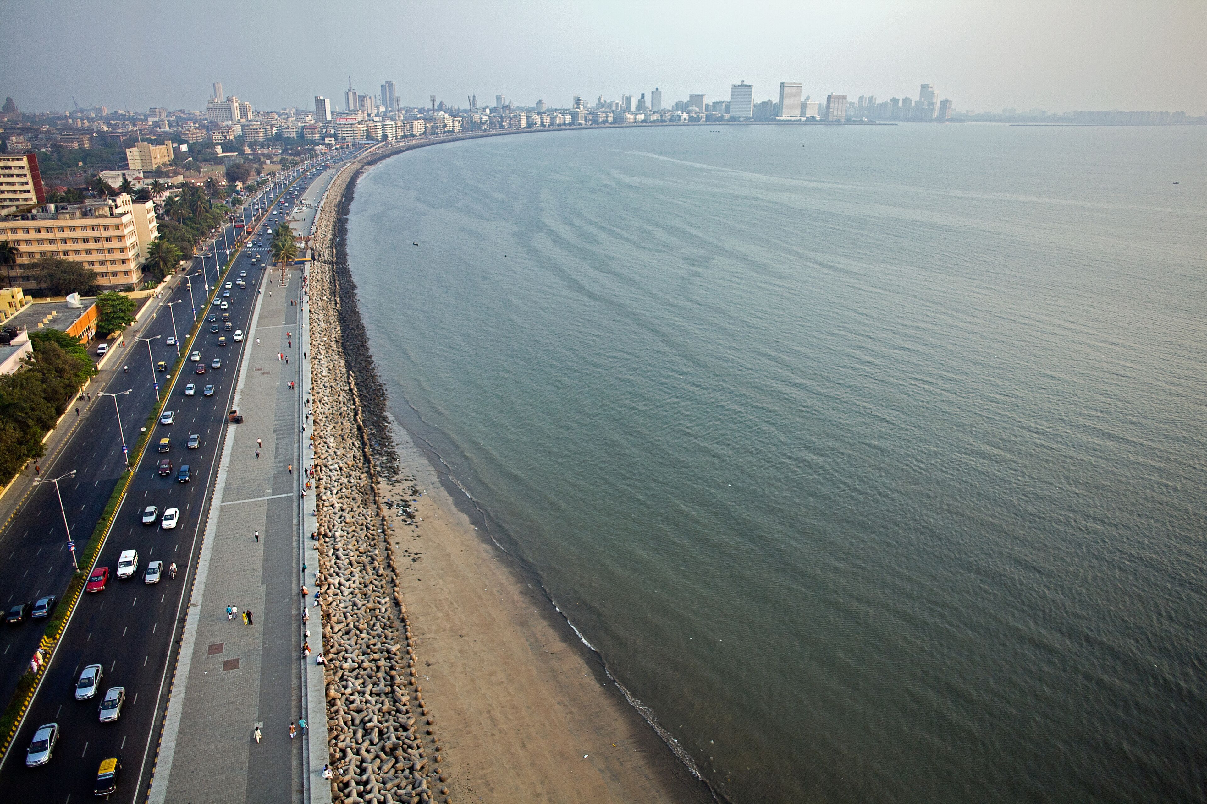 Uma estrada costeira com uma praia de um lado e o horizonte de uma cidade ao longe.