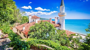Uma cidade costeira com um farol imponente, edifícios com telhados de terracota e vegetação exuberante.