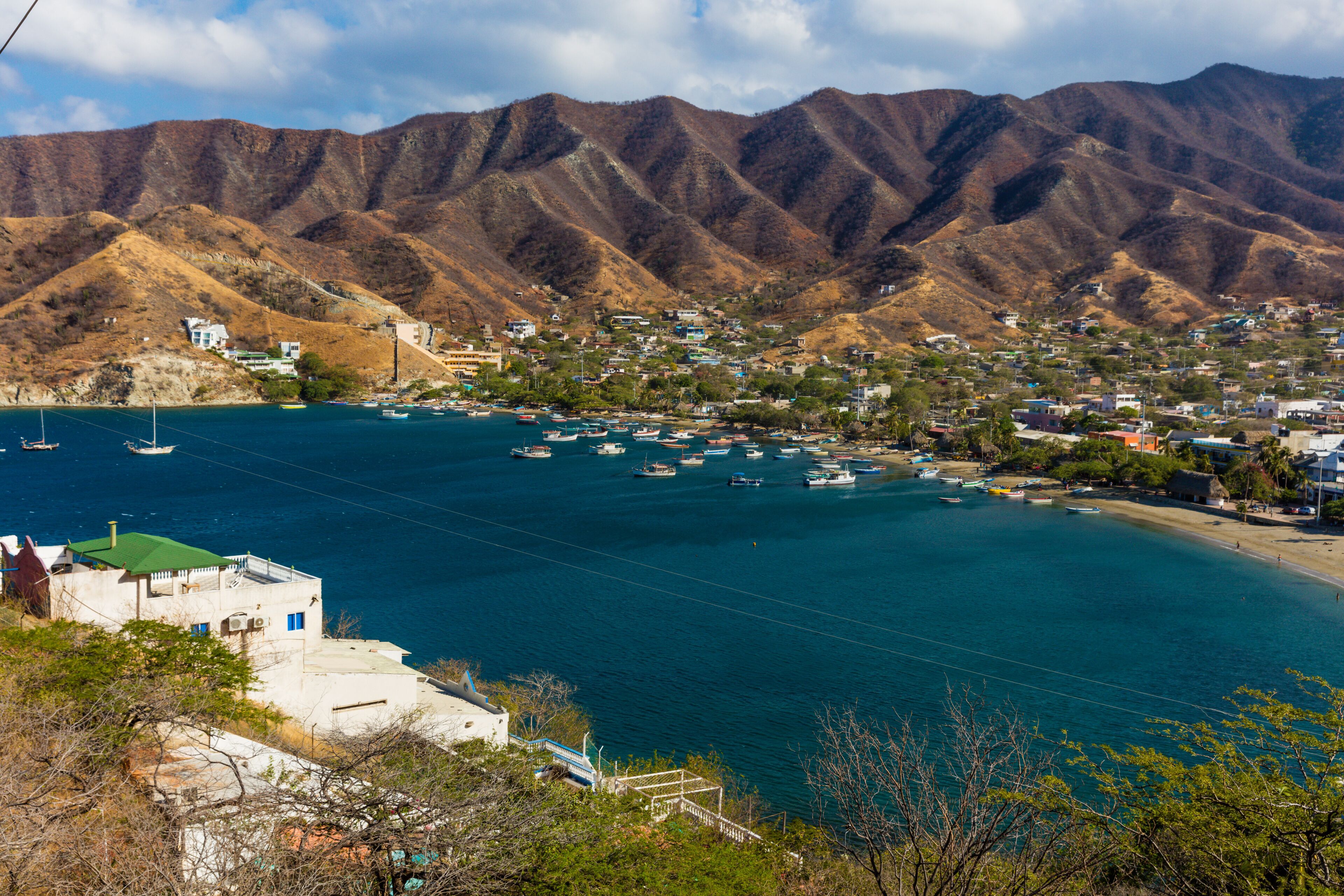 Uma vila costeira com montanhas ao fundo, barcos na água e casas ao longo da costa.