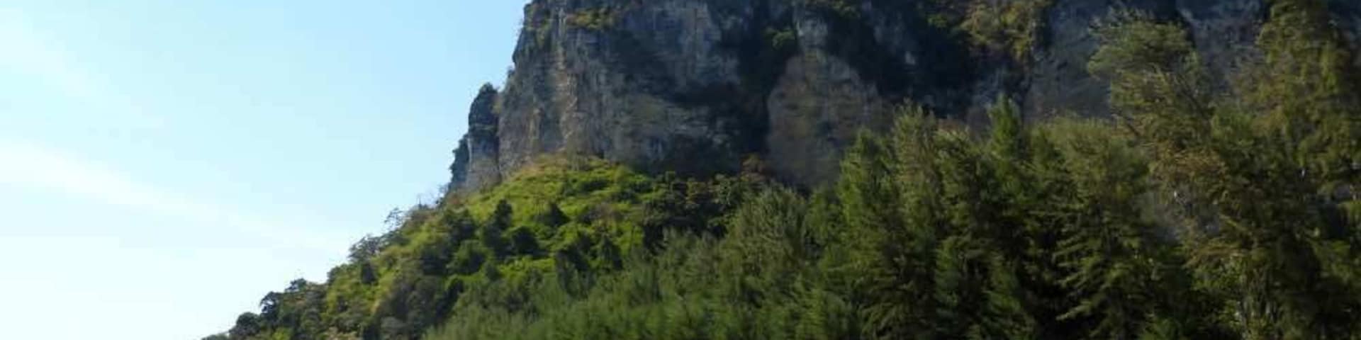 Uma praia com águas turquesa cristalinas, areia branca e um grande penhasco coberto de vegetação verde densa.