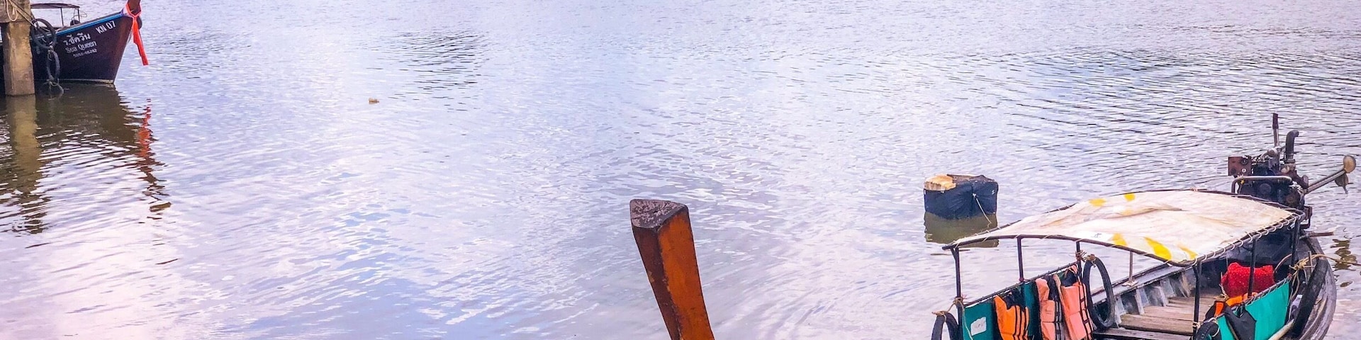 Um lago tranquilo com barcos, um cais de madeira e uma ilha arborizada ao fundo.