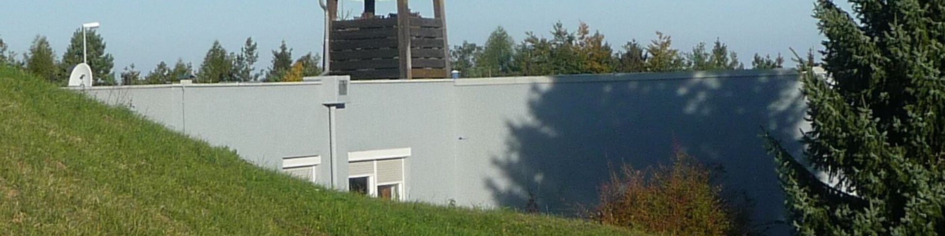 Uma colina coberta de grama com um pequeno edifício com uma cruz no topo, provavelmente uma capela ou memorial.
