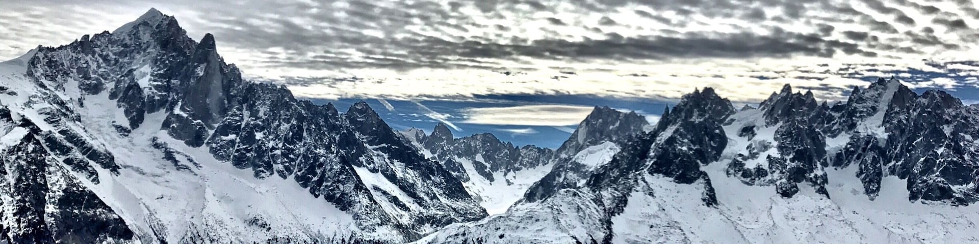 Cordilheira coberta de neve com um vale e uma estrada serpenteando por ele.