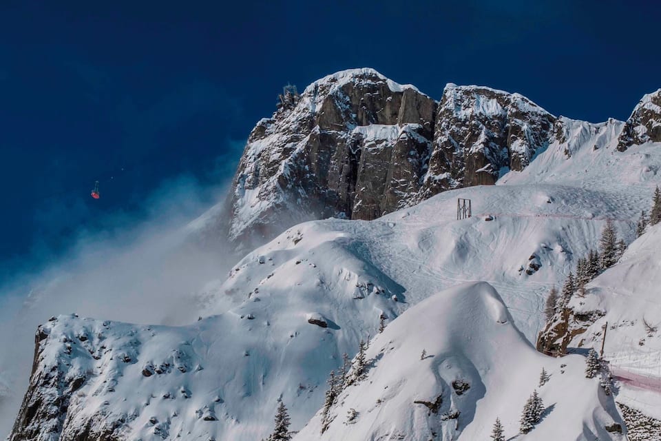 Montanha coberta de neve com afloramentos rochosos e um céu azul límpido.