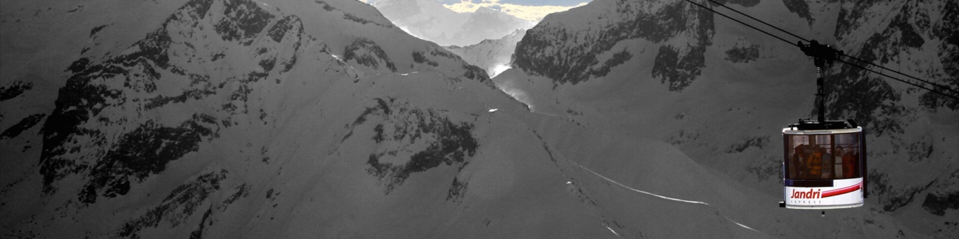 Teleférico em paisagem montanhosa com picos cobertos de neve e céu claro.