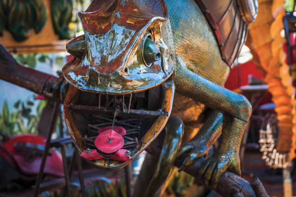 Uma grande escultura de sapo metálico com uma cesta pendurada na boca.