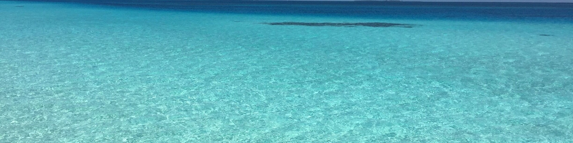 Mar azul-turquesa transparente com fundo de areia e horizonte distante.