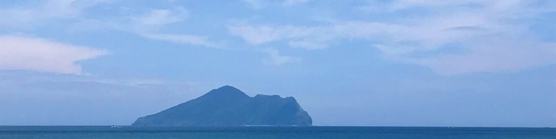 Uma praia com ondas, pessoas e uma montanha ao longe.