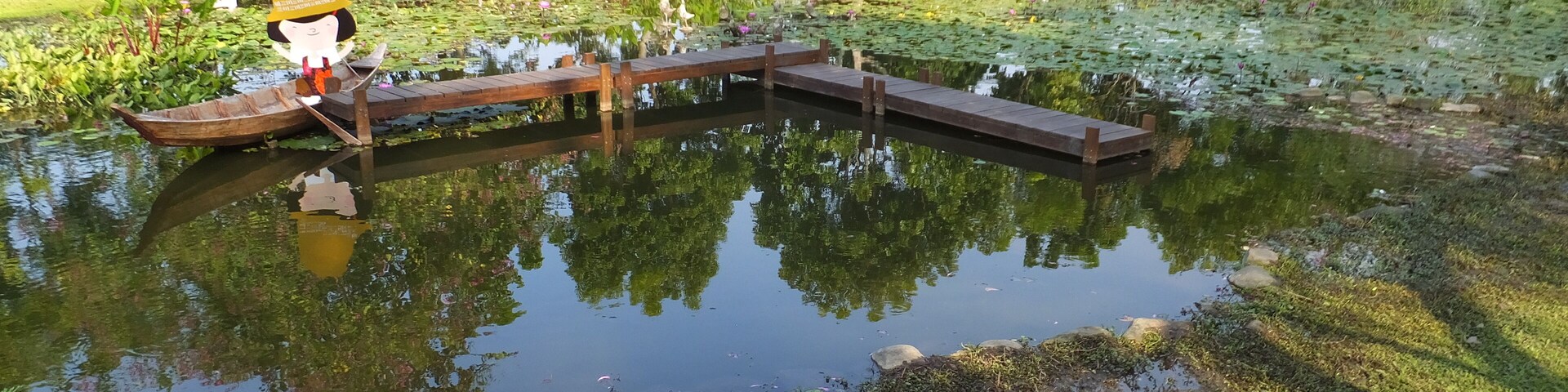 Um lago com um píer de madeira, rodeado por vegetação exuberante e plantas floridas.