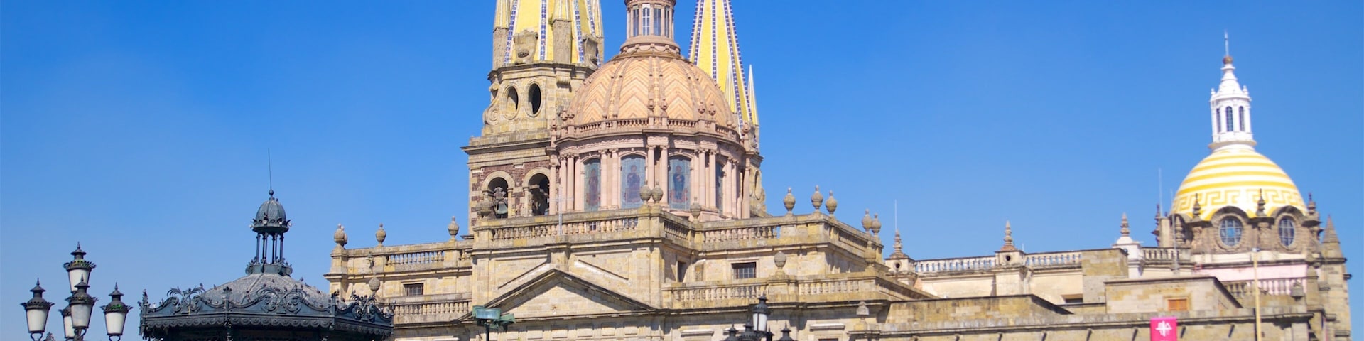 Uma catedral histórica com várias torres e uma cúpula imponente, rodeada por uma praça pública com pessoas e árvores.