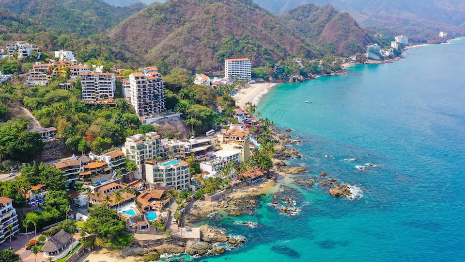 Uma cidade costeira com edifícios, uma praia e montanhas ao fundo.