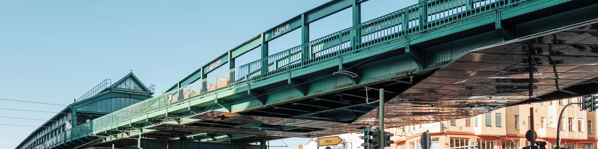 Uma ponte verde para pedestres sobre um cruzamento movimentado, com ciclistas e pessoas a pé.