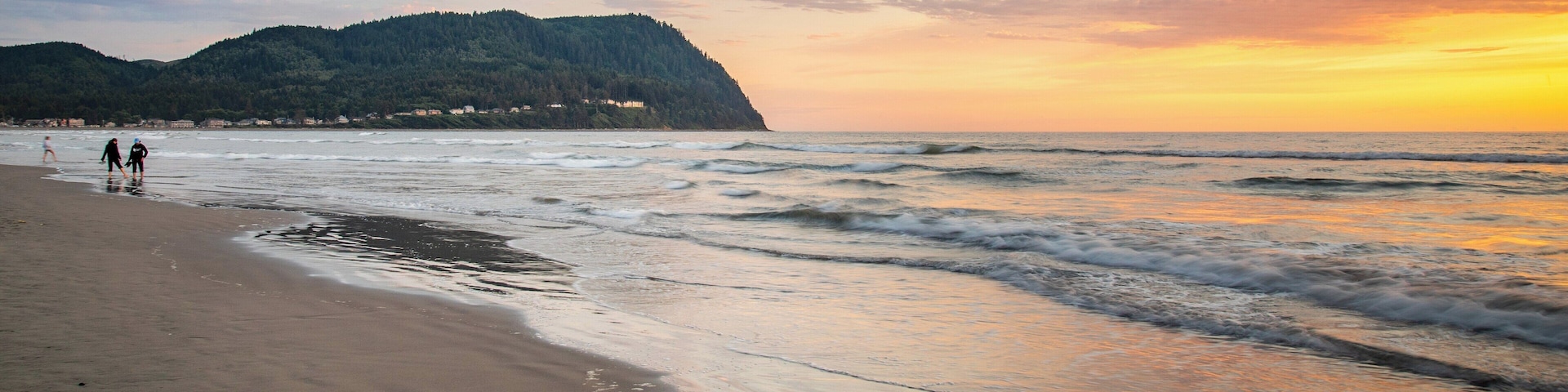 Uma praia com ondas, uma colina arborizada e um pôr do sol.
