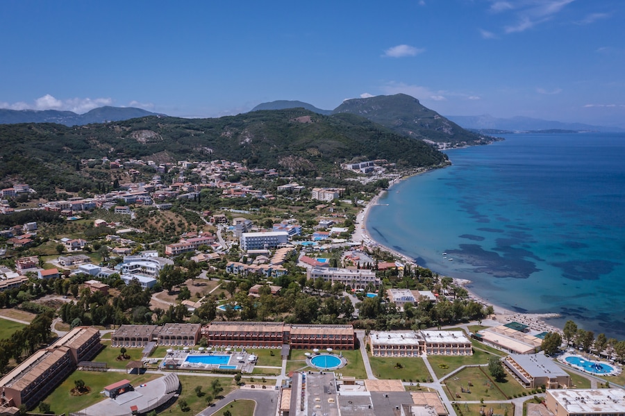 Vista aérea de uma cidade costeira com praia, montanhas e um complexo de piscinas.