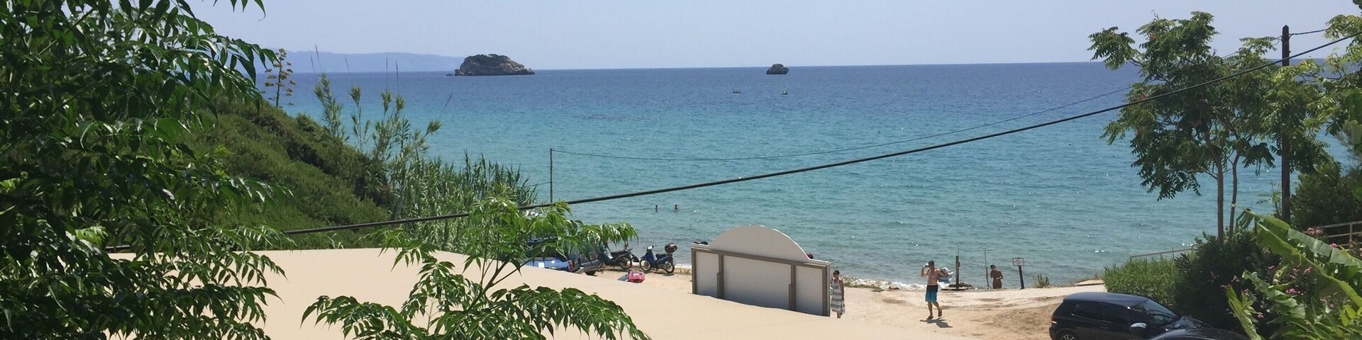 Uma praia com areal, uma construção pequena e um barco na água.