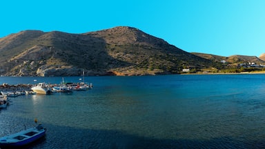 Um lago tranquilo com barcos atracados à esquerda, rodeado por colinas rochosas e edifícios brancos.