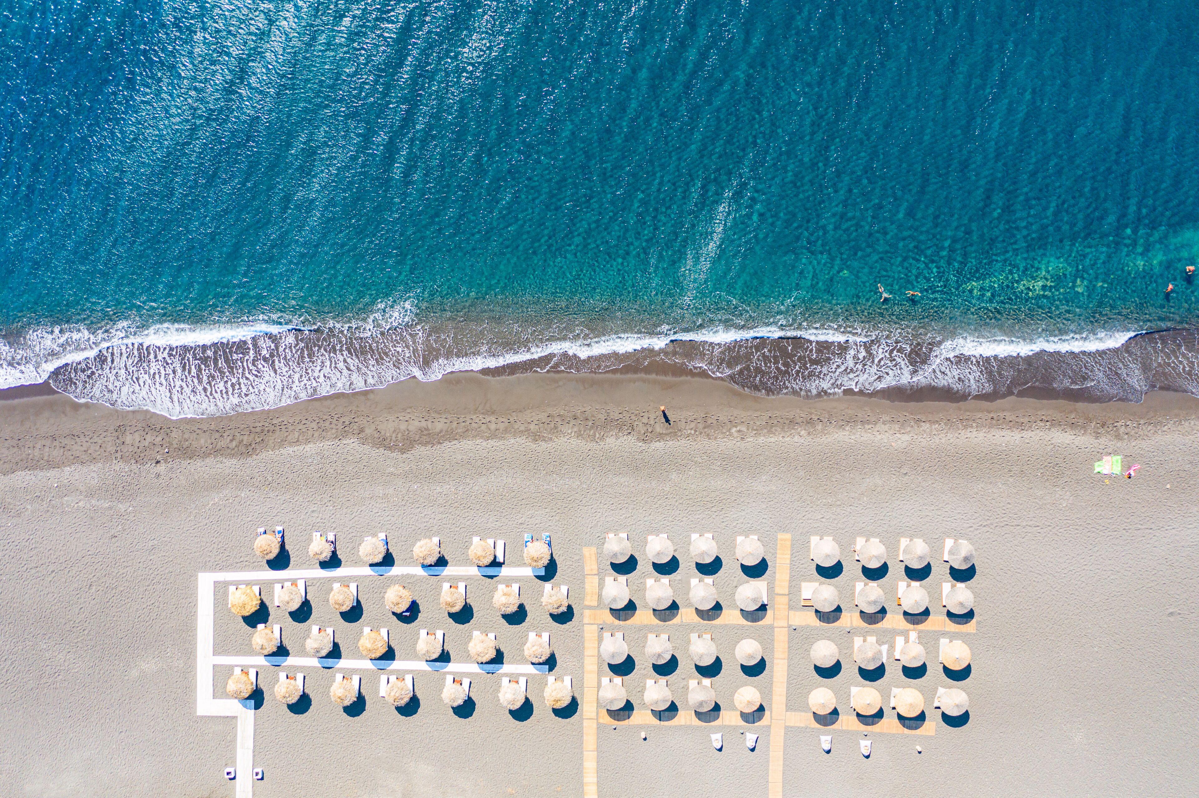 Vista aérea de uma praia com fileiras de guarda-sóis e cadeiras de praia.