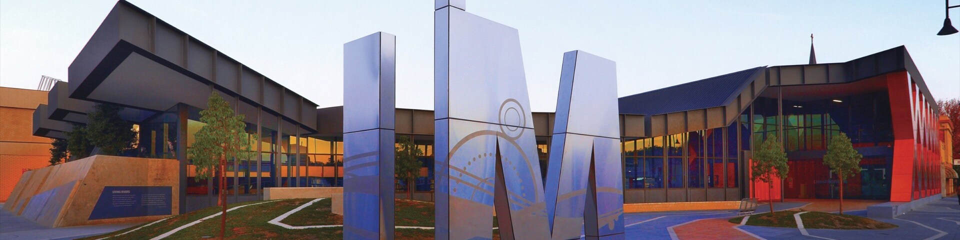 Um complexo moderno de edifícios com painéis de vidro refletivos e uma escultura central.