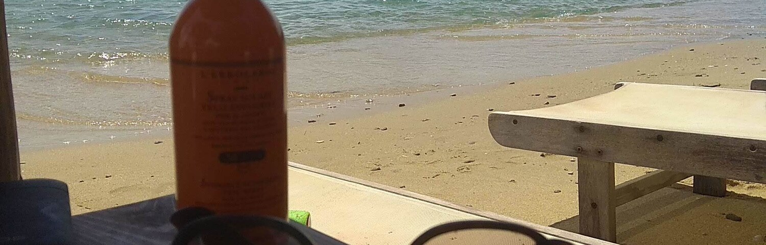 Uma praia com uma mesa de madeira, uma garrafa e óculos de sol.