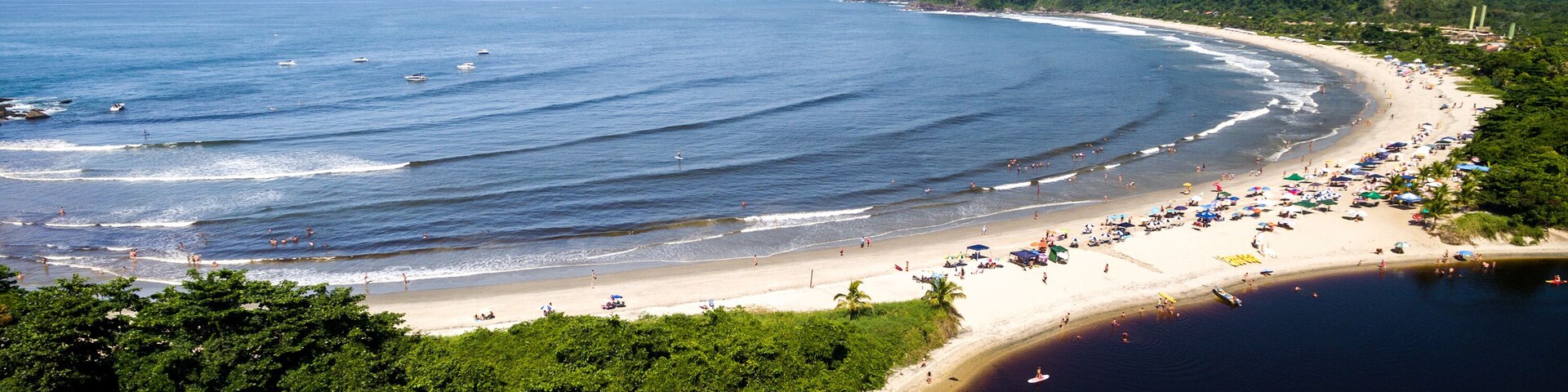 Uma praia com ondas, areal arenoso e um morro coberto de árvores.