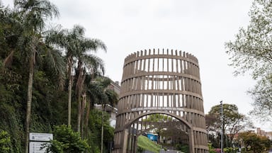Um arco de madeira com uma placa indicando 'Bento Goncalves' e uma estrada que atravessa uma área verde com árvores.