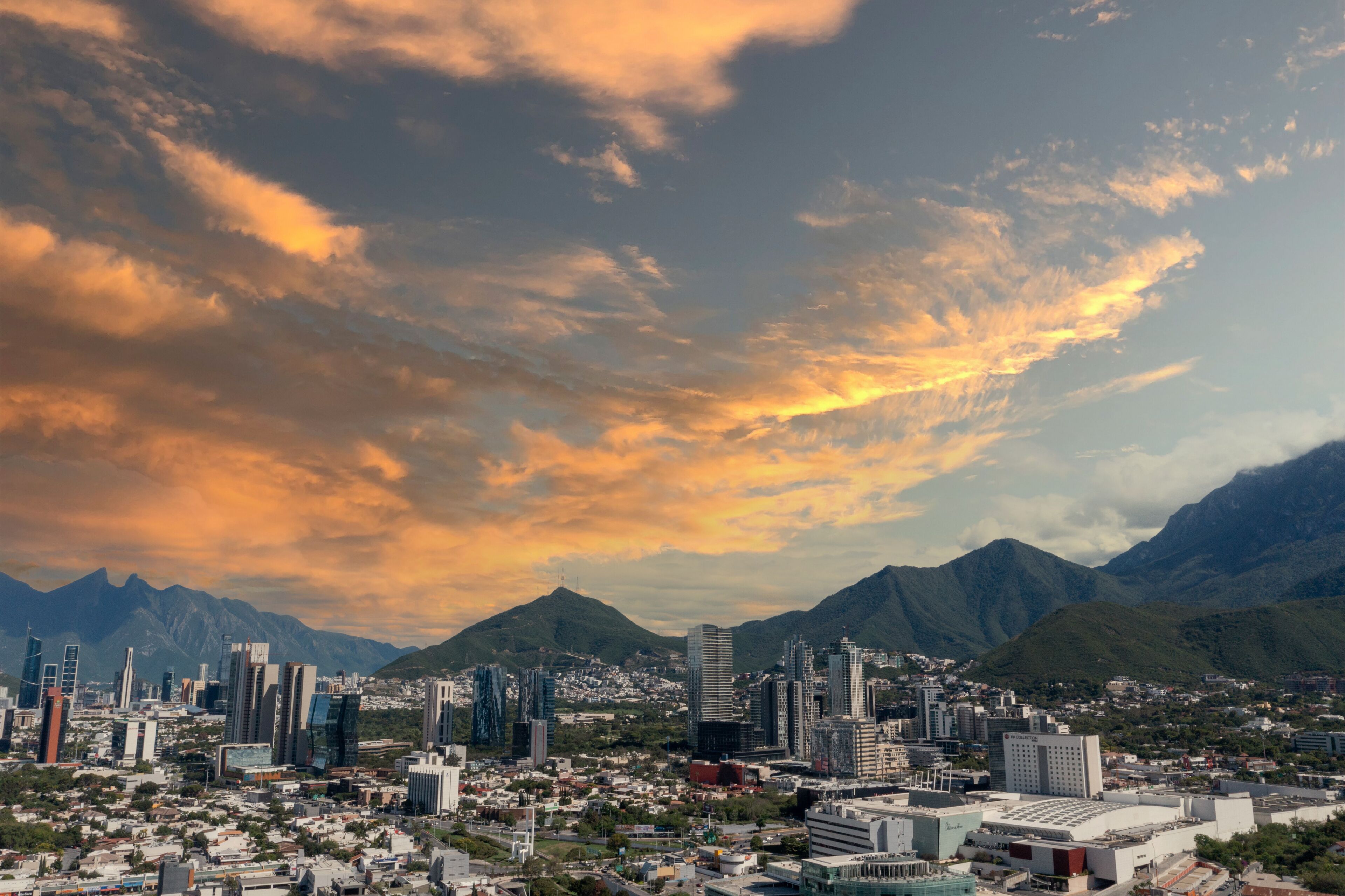 Paisagem urbana com edifícios modernos, uma cordilheira e um céu ao pôr do sol.