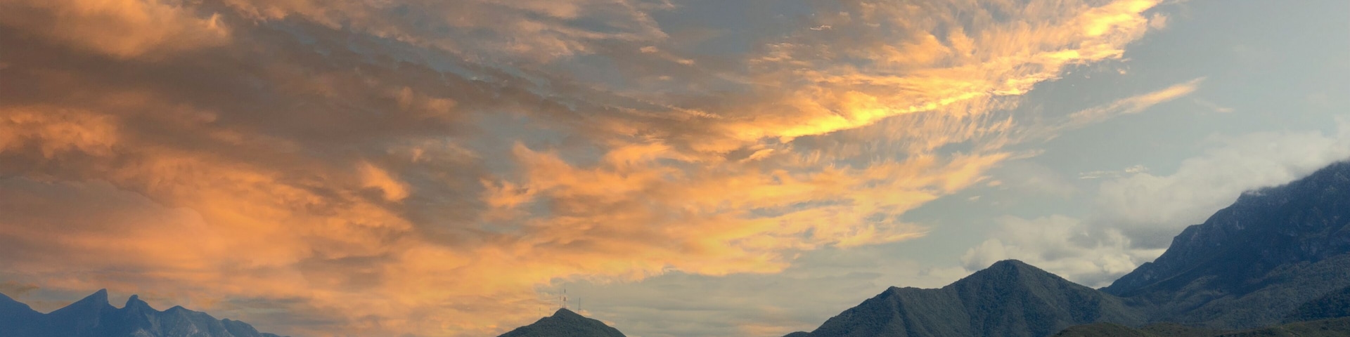 Paisagem urbana com edifícios modernos, uma cordilheira e um céu ao pôr do sol.