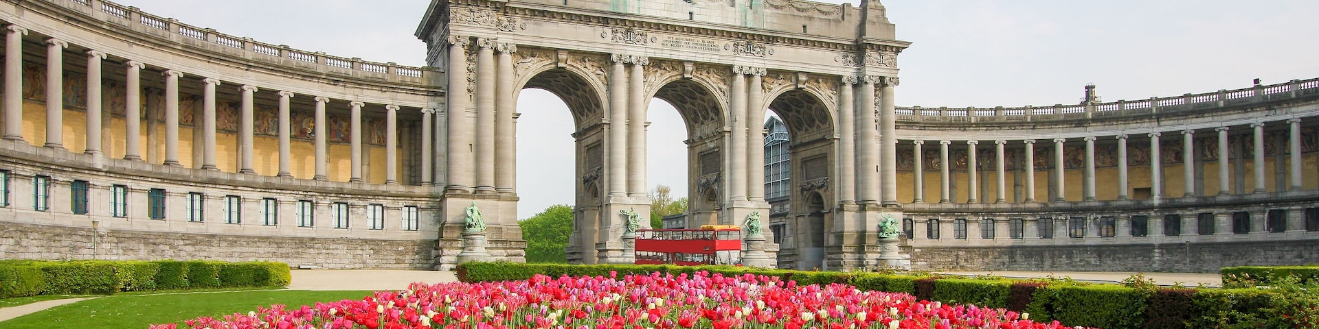 Um edifício imponente com um arco central e um campo de tulipas vibrantes ao primeiro plano.
