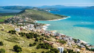 Uma vila costeira com edifícios ao longo da orla marítima, vista nítida do mar e colinas ondulantes ao fundo.