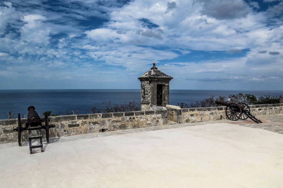 Uma fortaleza costeira com canhões, uma pequena torre e vista ampla do oceano.