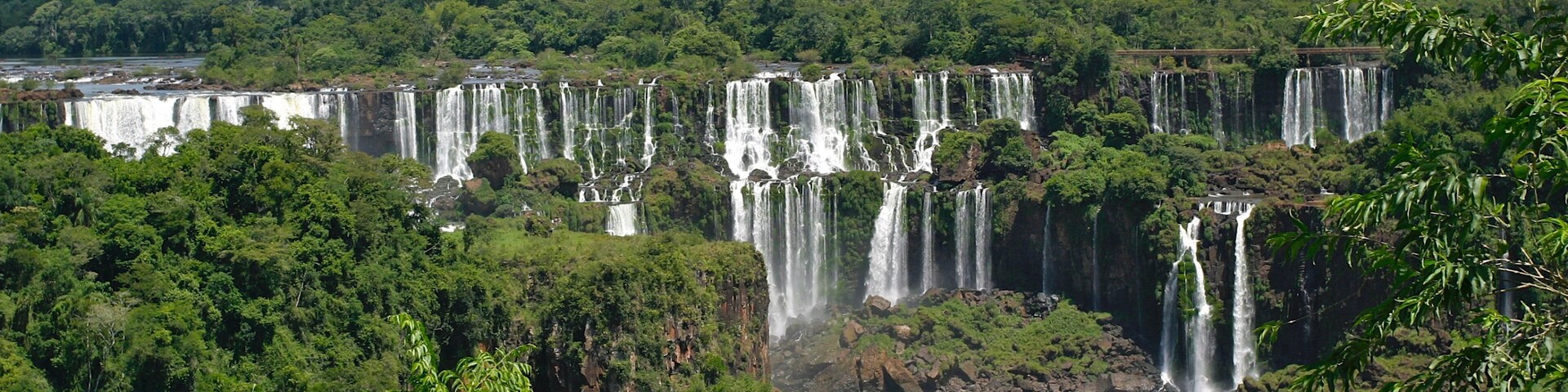 Uma série de cascatas descendo por uma paisagem verde e exuberante, com um rio em primeiro plano.