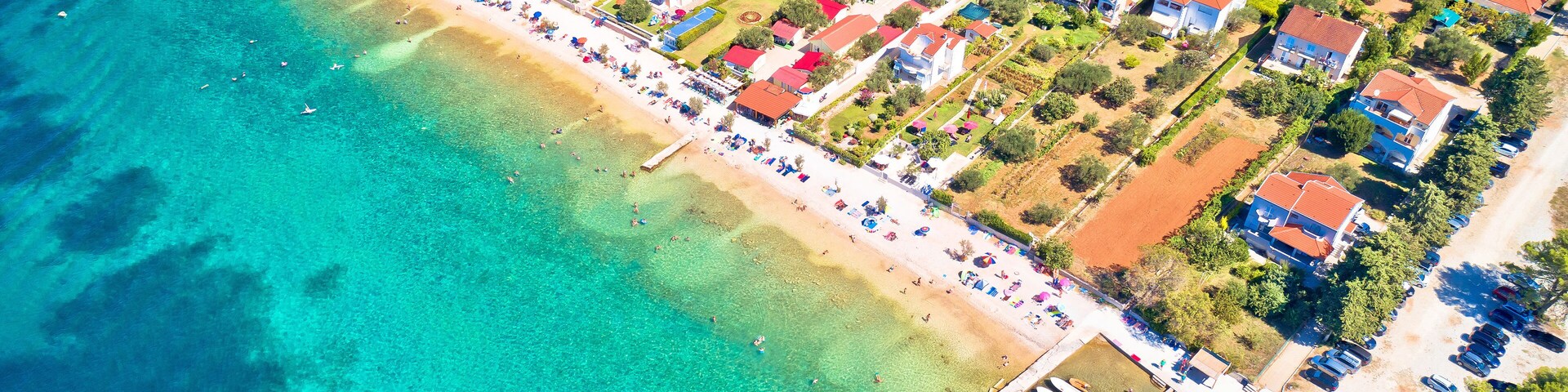Vista aérea de uma cidade costeira com praia, águas turquesa cristalinas e casas coloridas.