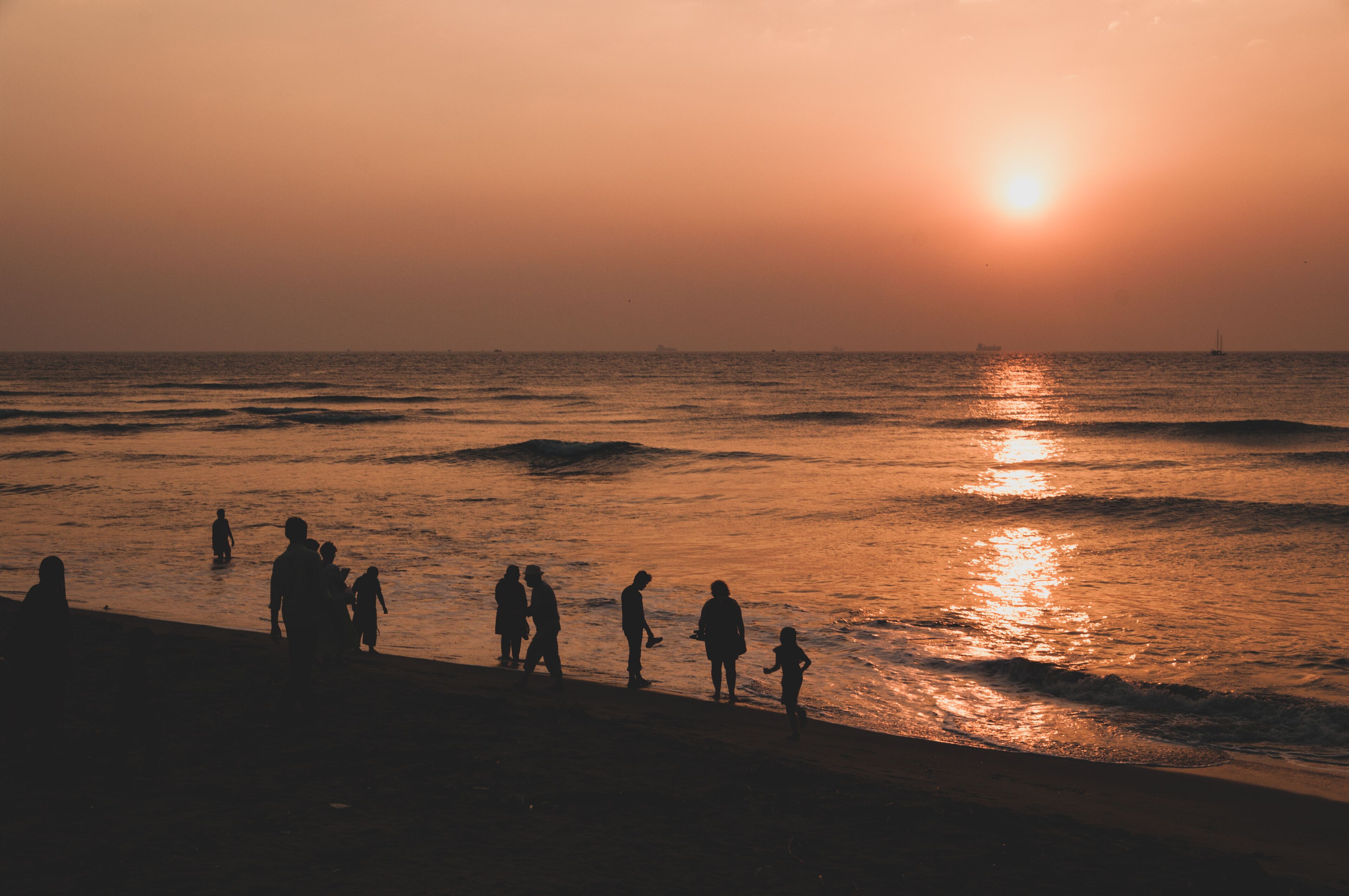 Um pôr do sol sobre o oceano, com silhuetas de pessoas na praia.