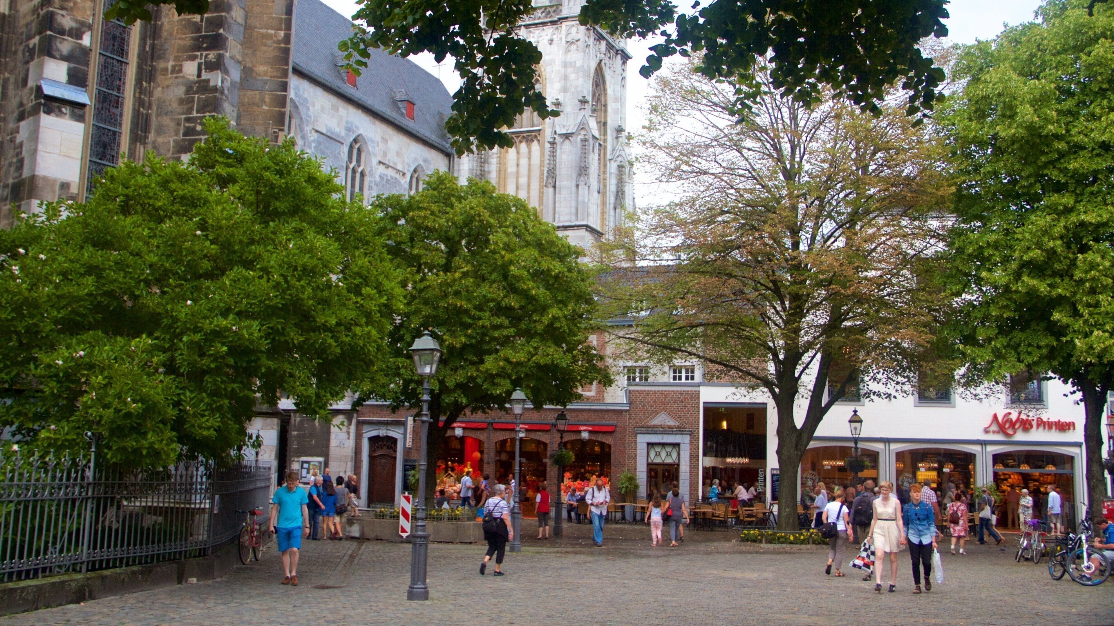 Uma praça movimentada com edifícios históricos, uma igreja imponente e diversas lojas.
