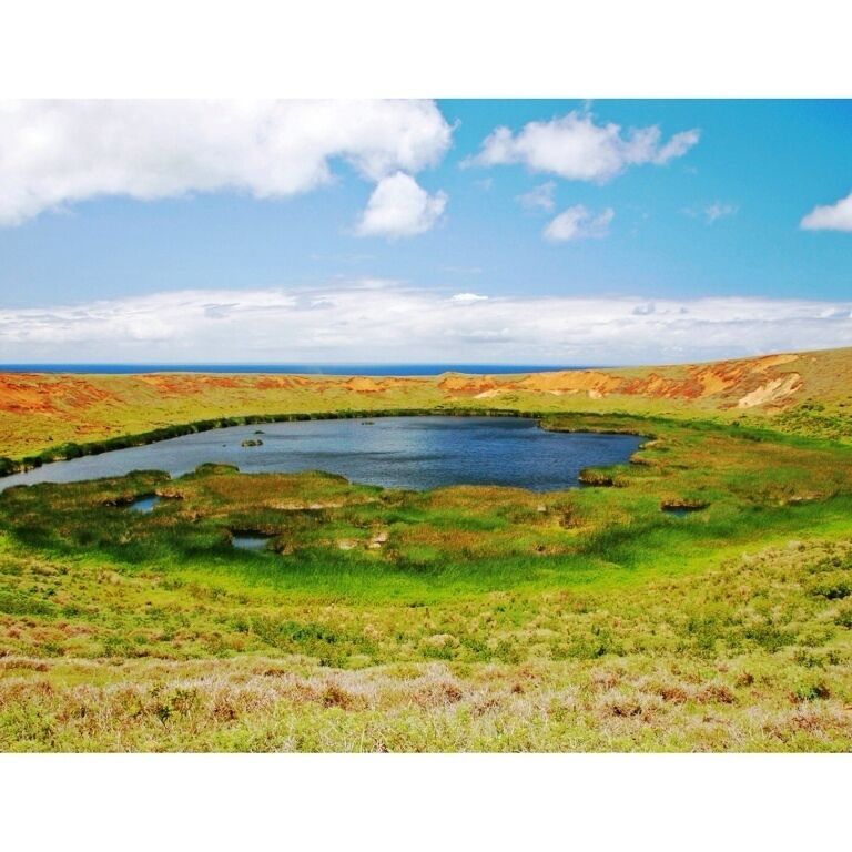 Um lago rodeado por colinas verdes e castanhas sob um céu limpo.
