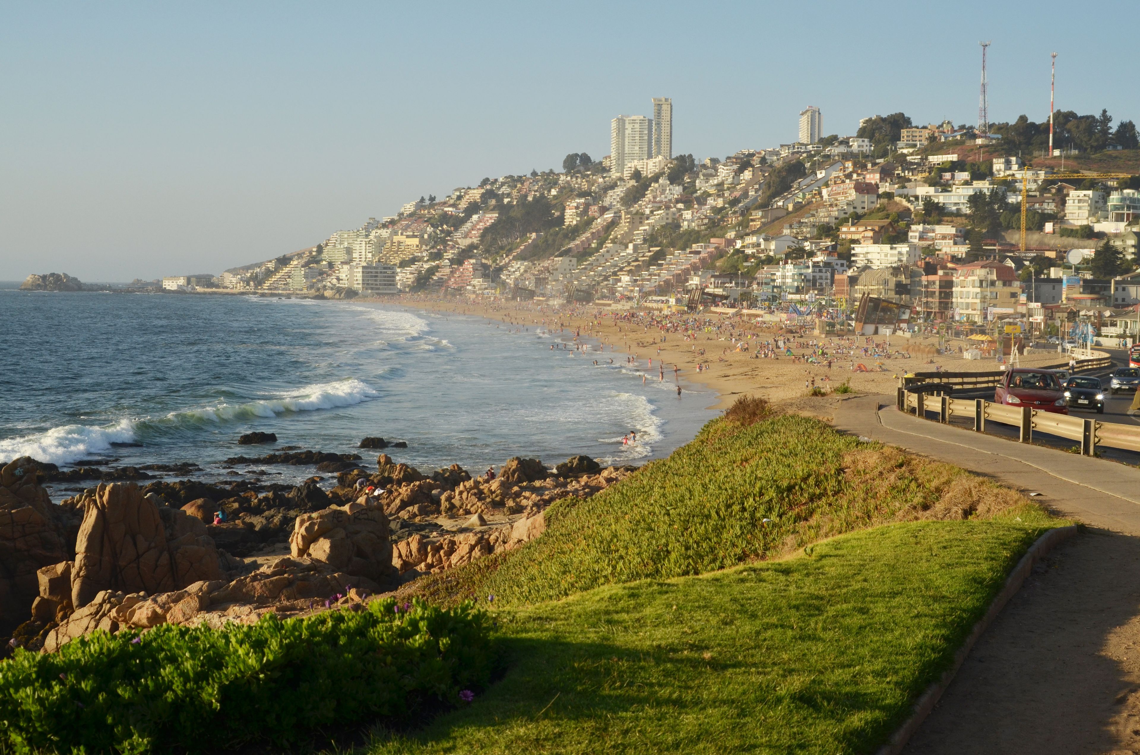 Paisagem costeira com praia, litoral rochoso e edifícios residenciais.