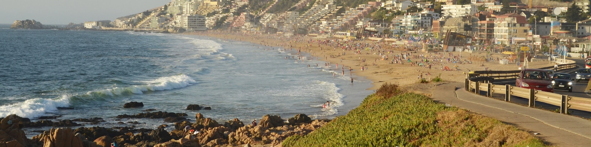 Paisagem costeira com praia, litoral rochoso e edifícios residenciais.