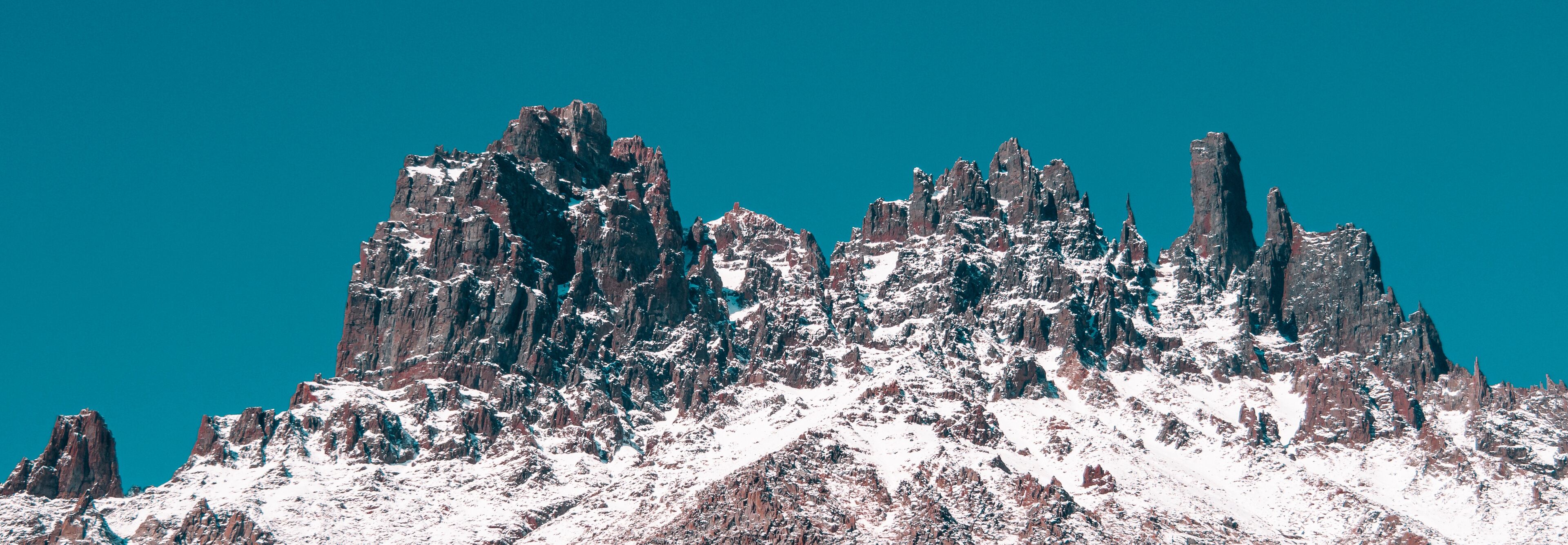 Pico de montanha coberto de neve com picos afiados e irregulares sob um céu azul límpido.