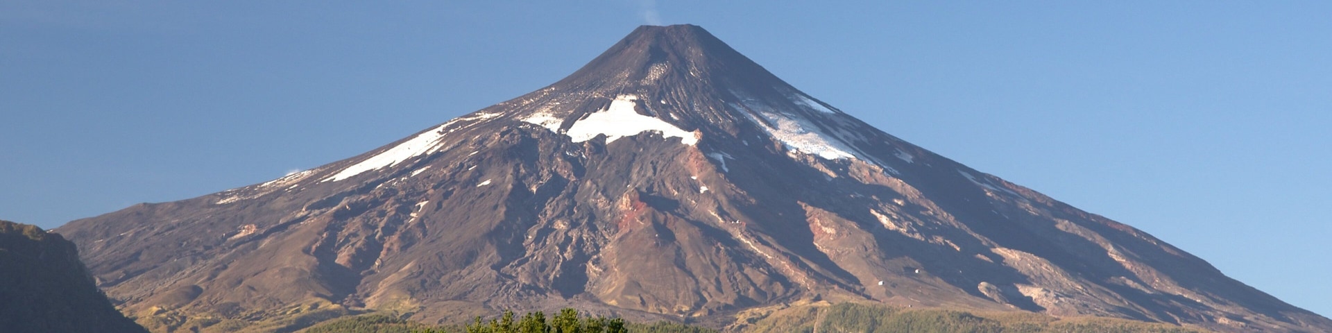 Montanha nevada com um vale florestado abaixo.
