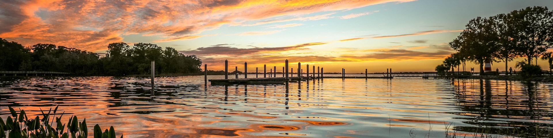 Um pôr do sol sobre um lago calmo, com um cais e árvores.