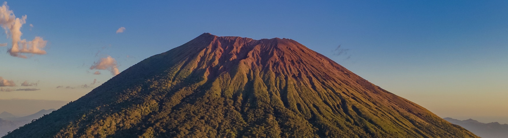 Um vulcão com encosta arborizada e céu limpo.