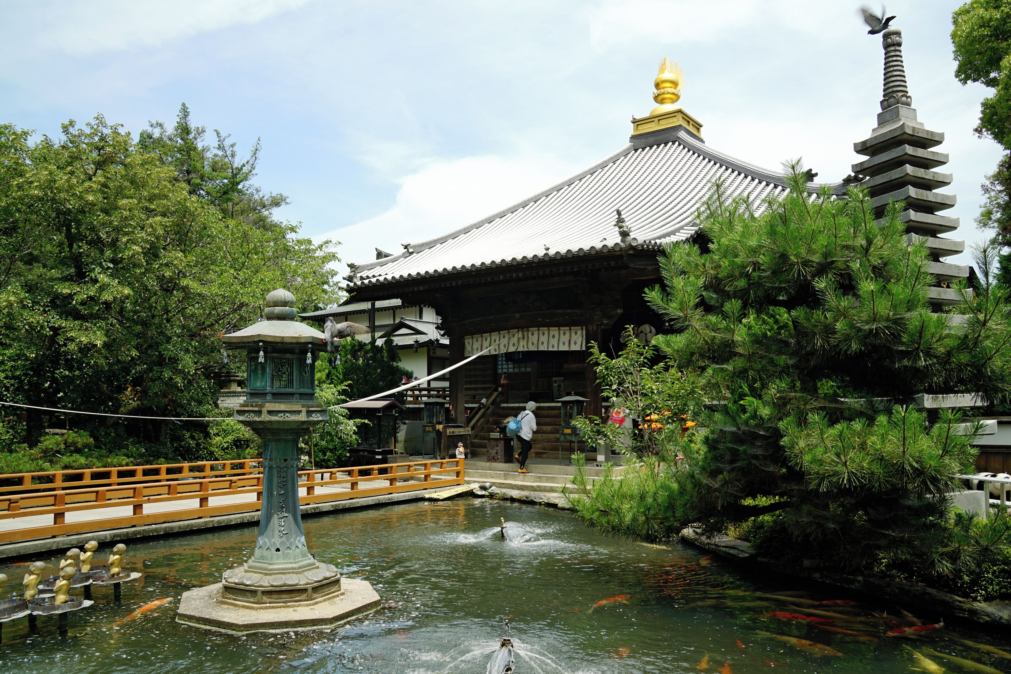 Um templo japonês tradicional com pagode, lago com carpas e uma ponte.