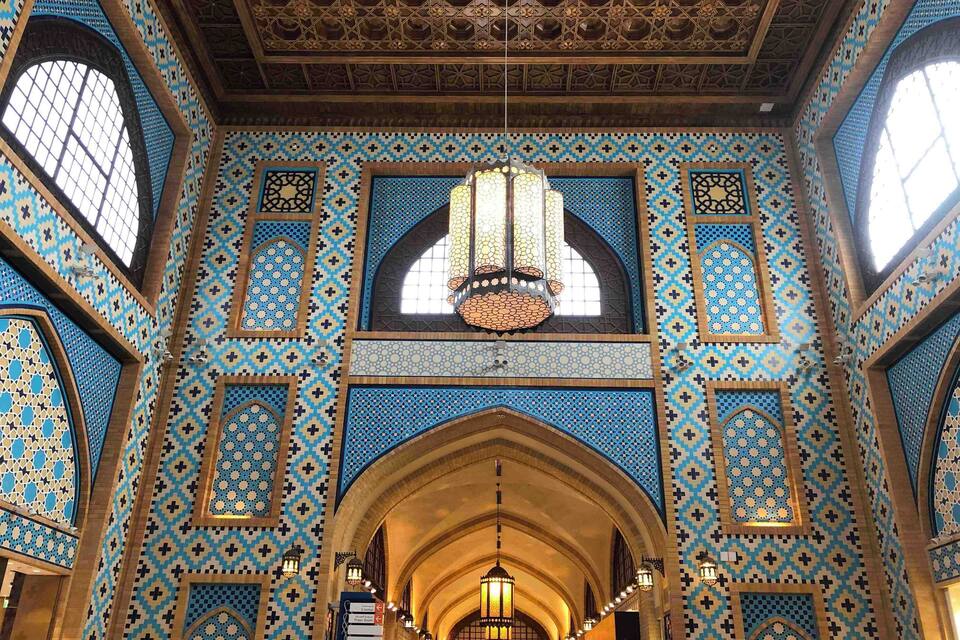 Um salão imponente com intrincados padrões de azulejos azul e bege, grandes janelas em arco e lustres pendentes.