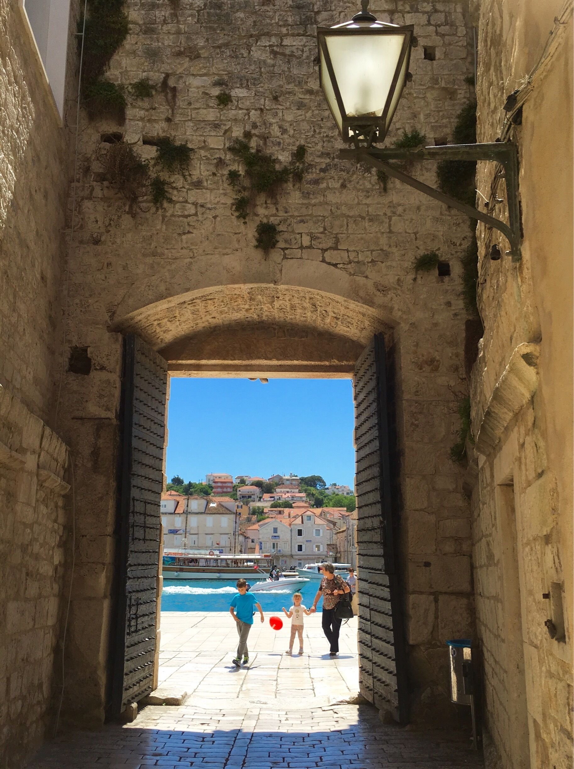 Um arco de pedra leva a um cais com edifícios ao fundo.