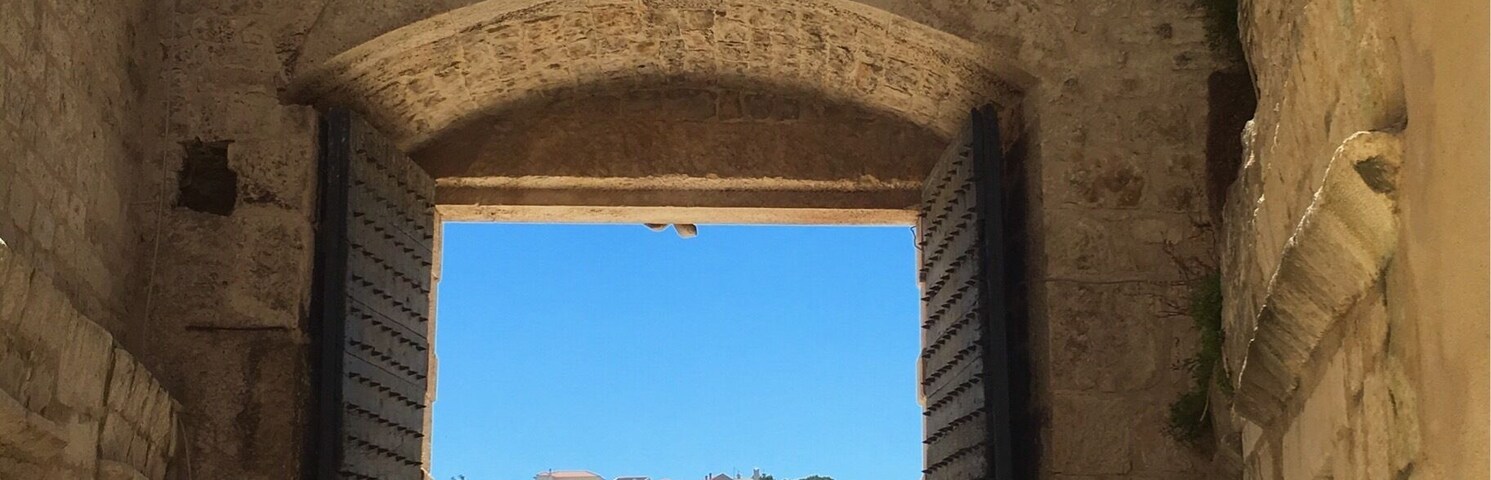Um arco de pedra leva a um cais com edifícios ao fundo.