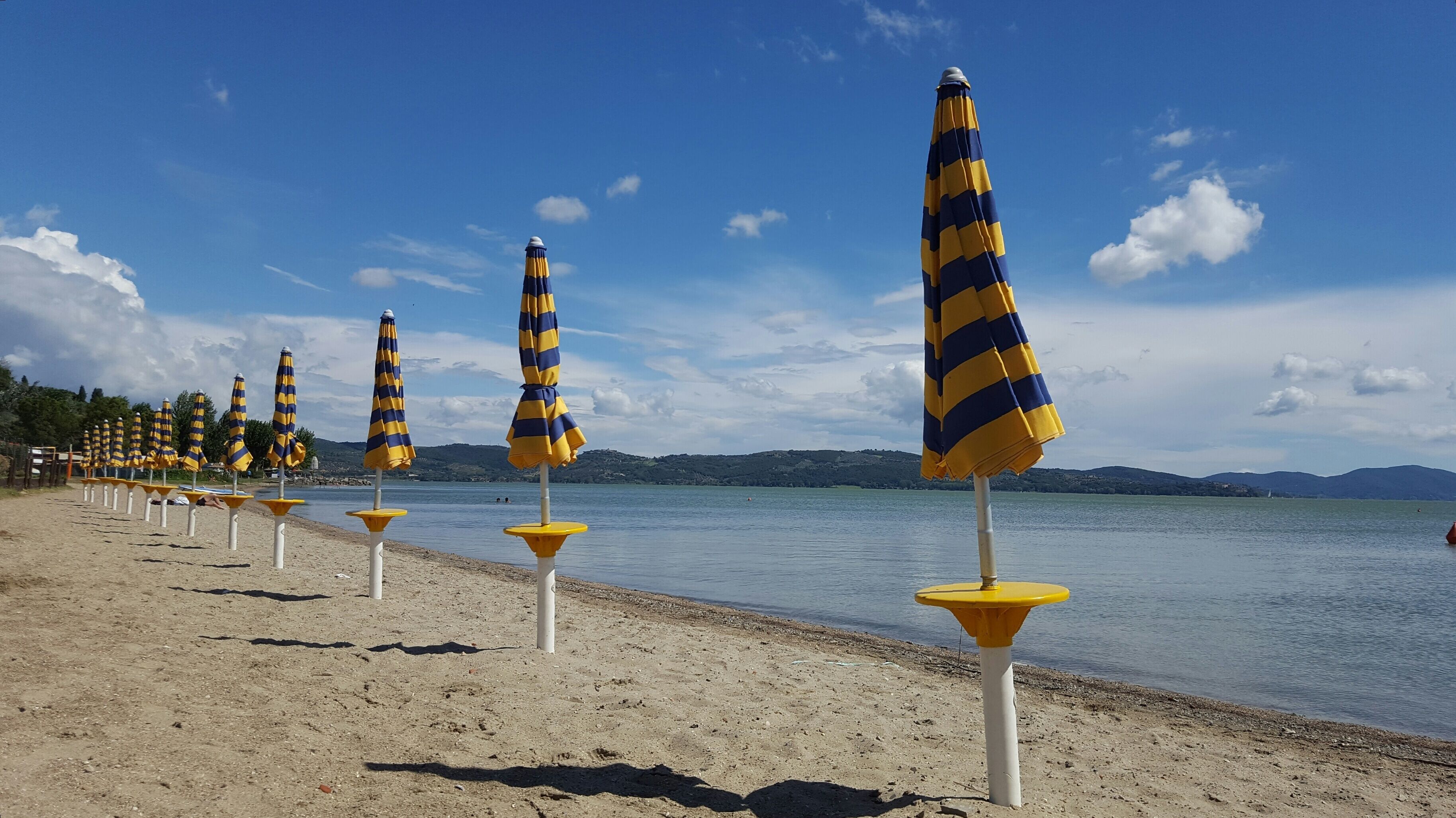 Uma praia com guarda-sóis listrados em amarelo e azul, alinhados na areia.