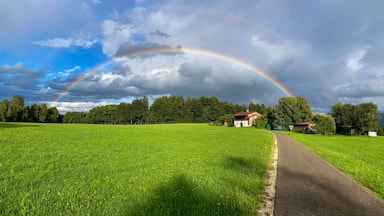 Um campo verdejante com um arco-íris sobre a paisagem rural.